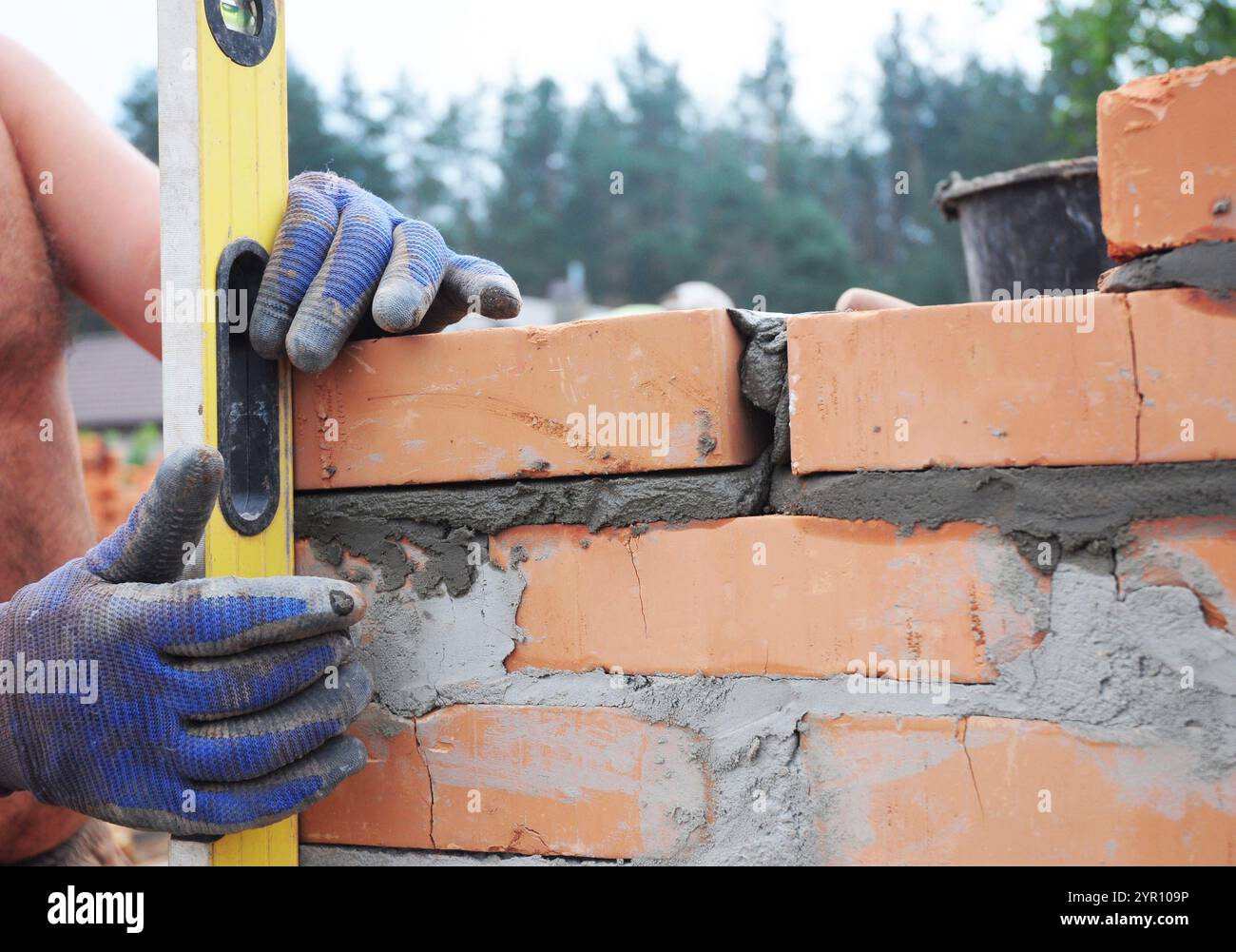 Bricklayer laying bricks and measuring brick wall with spirit level ...