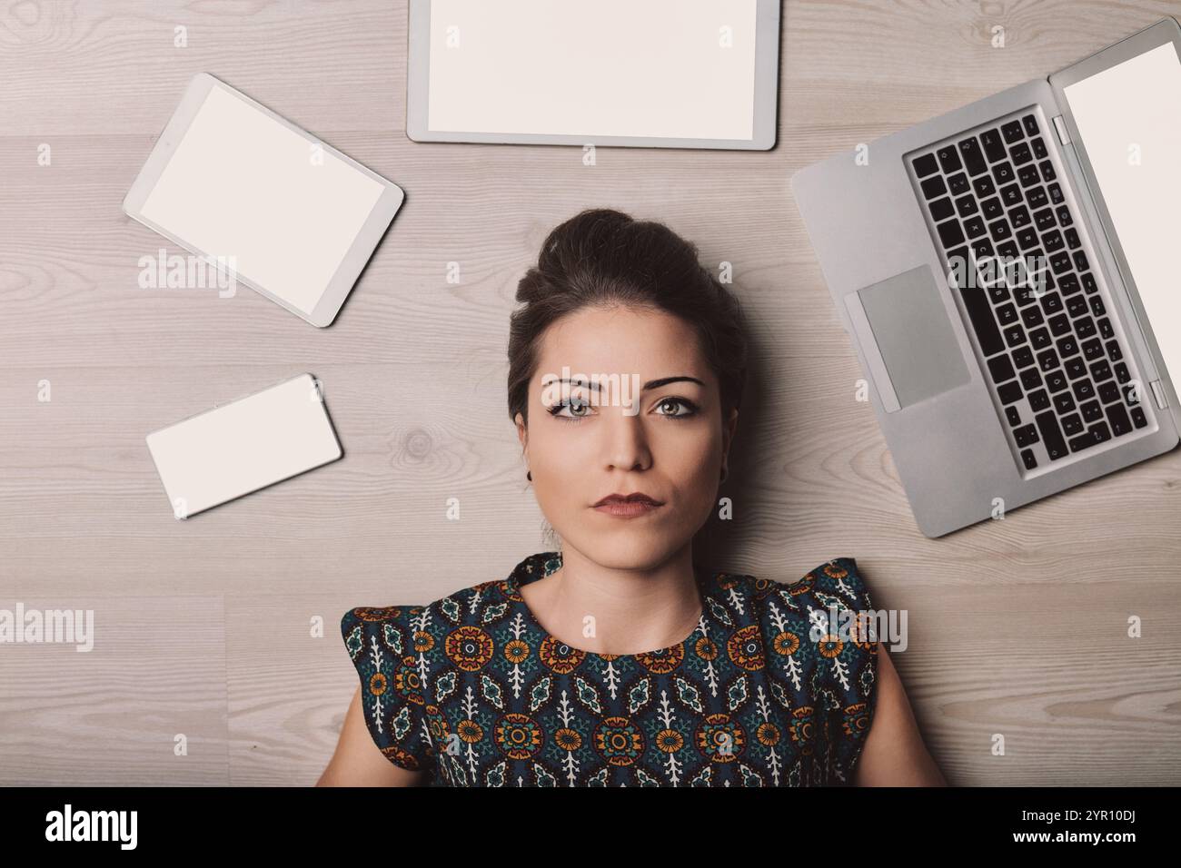 Young woman lies on a wood floor surrounded by digital devices with ...