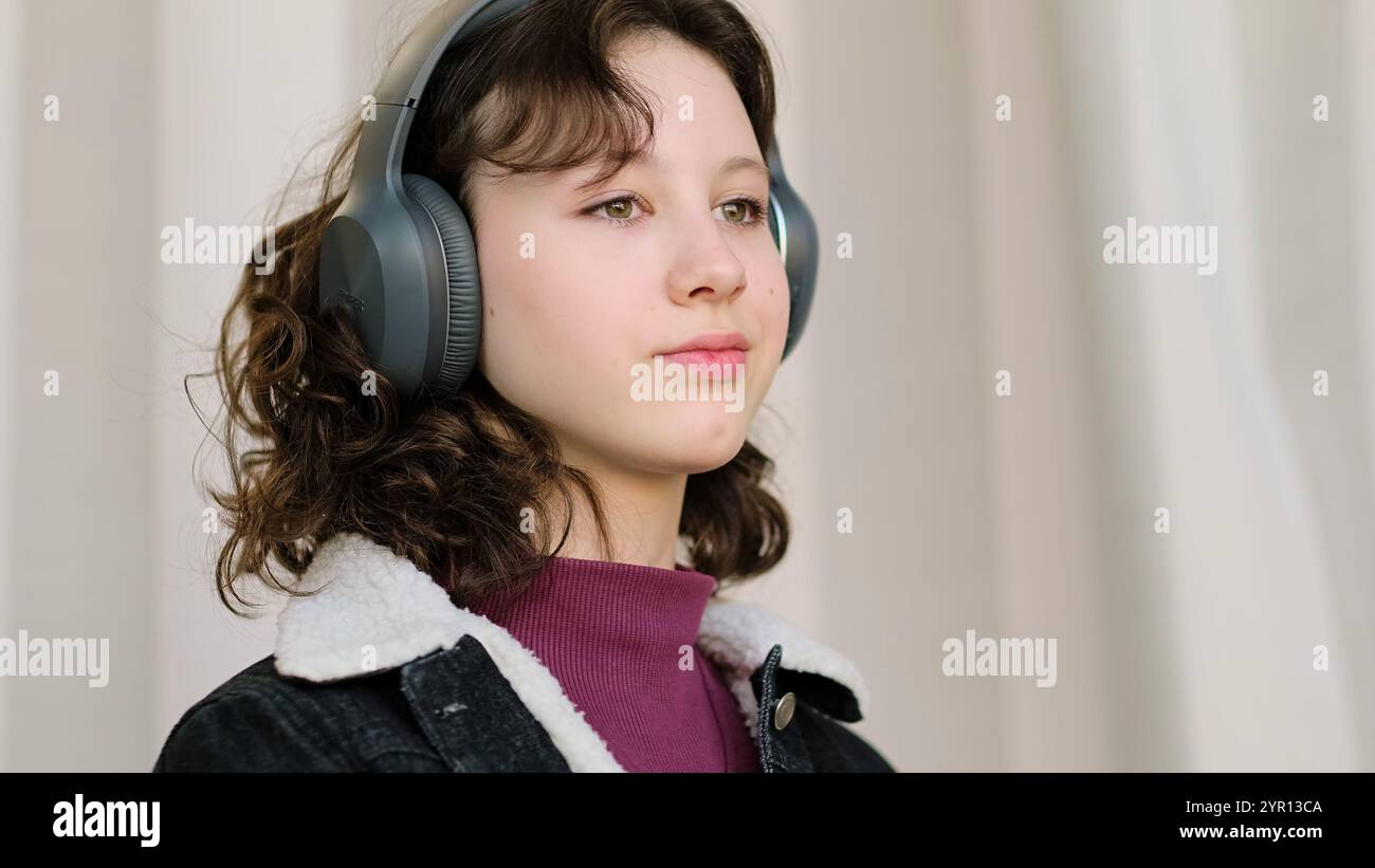 A reflective young girl listens through headphones, her gaze directed ...