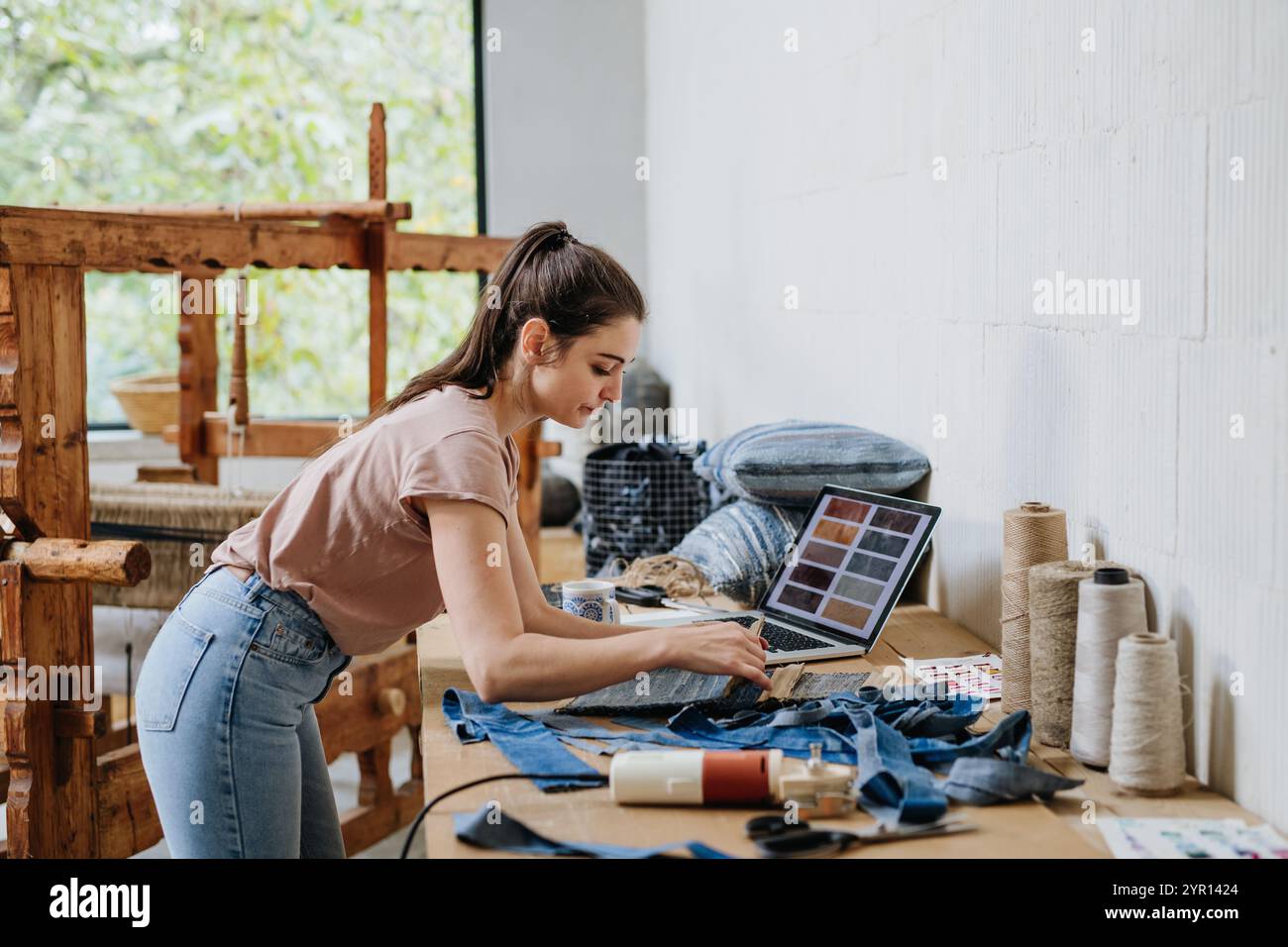 Young businesswoman working on laptop on workbench, standing by wooden ...