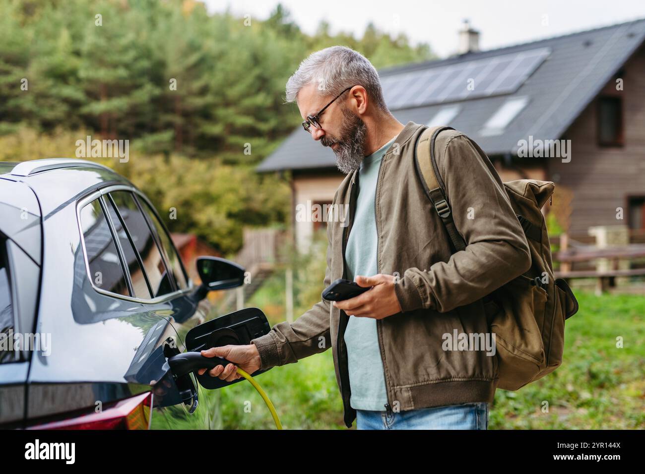 Man charging electric car in front of his house, plugging the charger ...