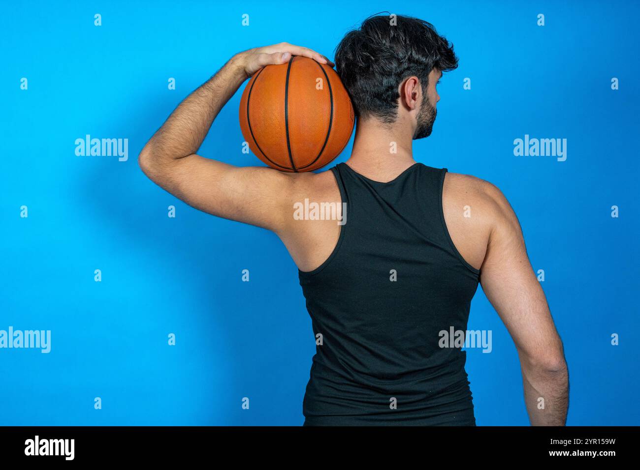 Male athlete holding a basketball on his shoulder, showcasing strength ...