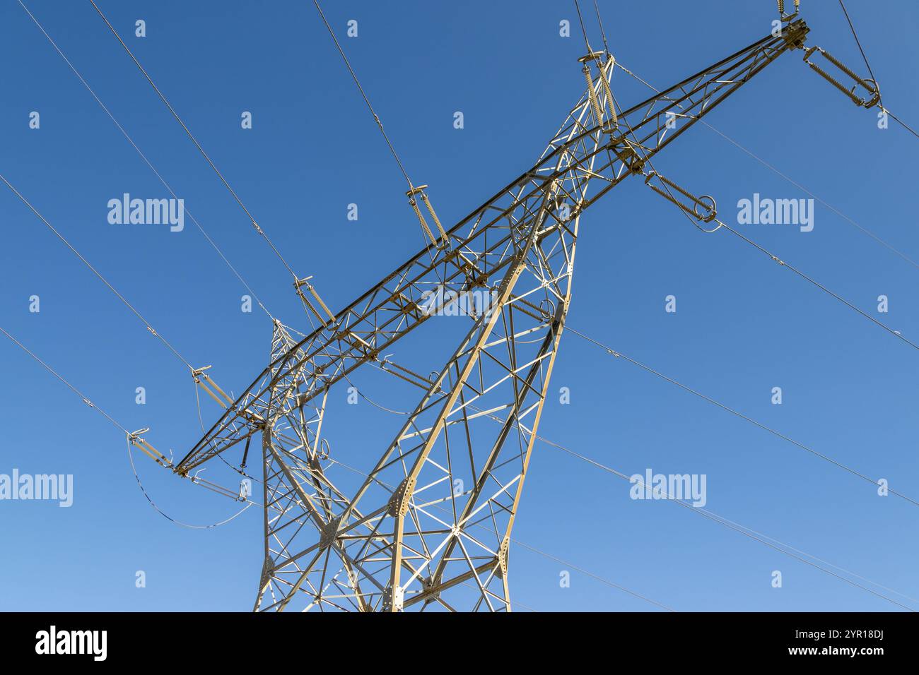 Metal electricity pylon carrying power lines against a clear blue sky ...