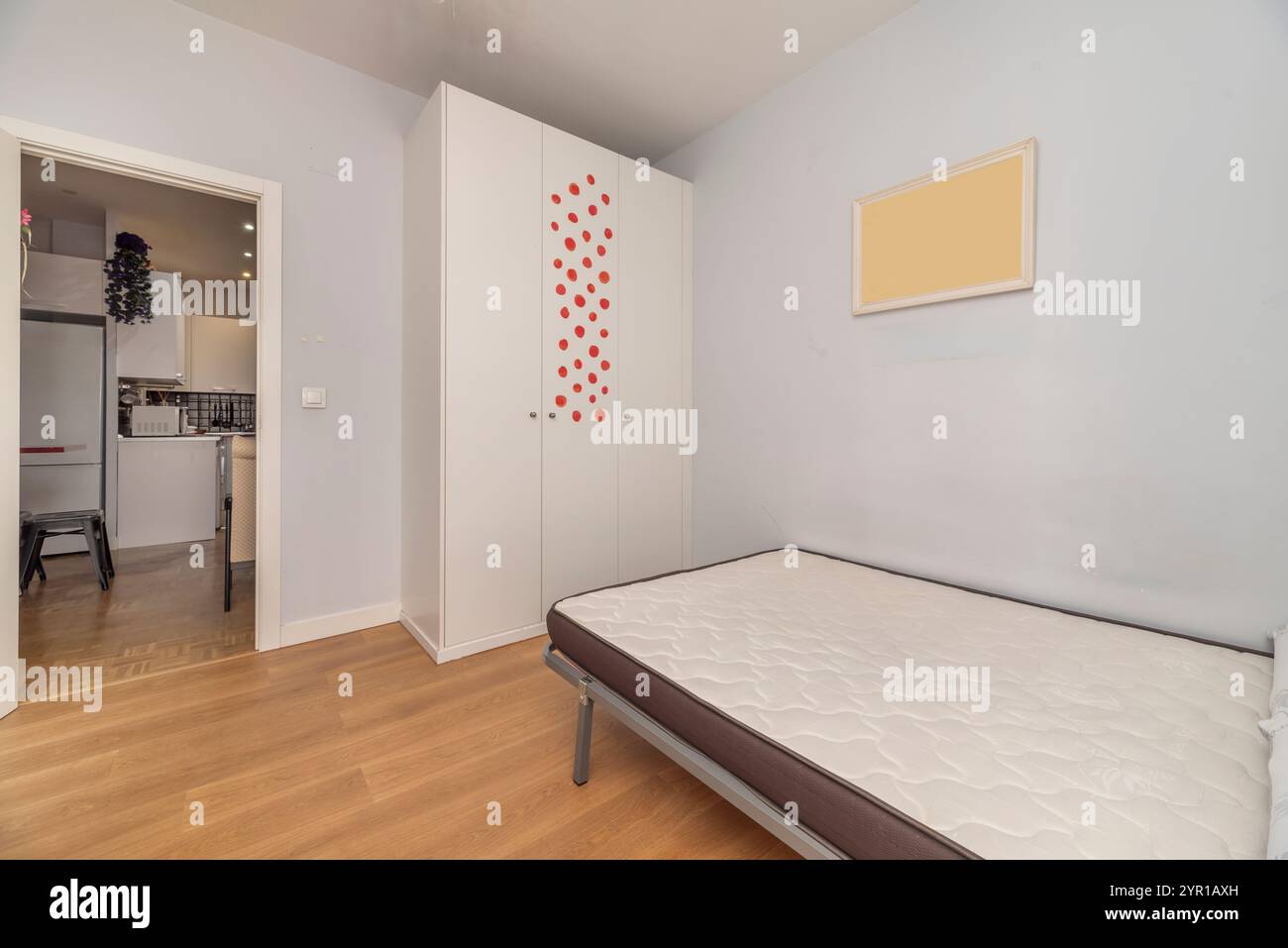 A bedroom with a custom-made white wardrobe and a bed with no sheets on ...