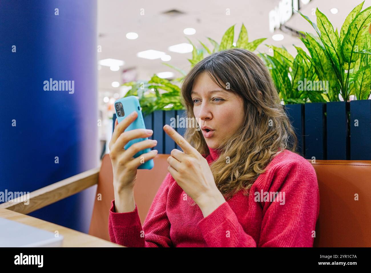 Young woman happily video-calling on her smartphone in a busy mall food ...