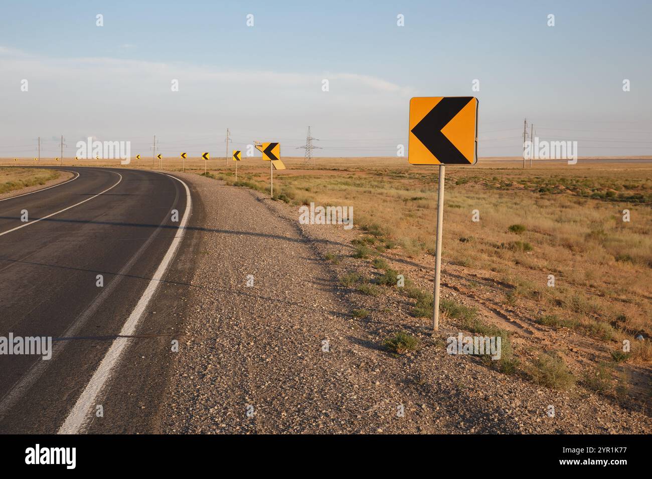 A winding asphalt road in Kazakhstan features sharp left turn signs ...