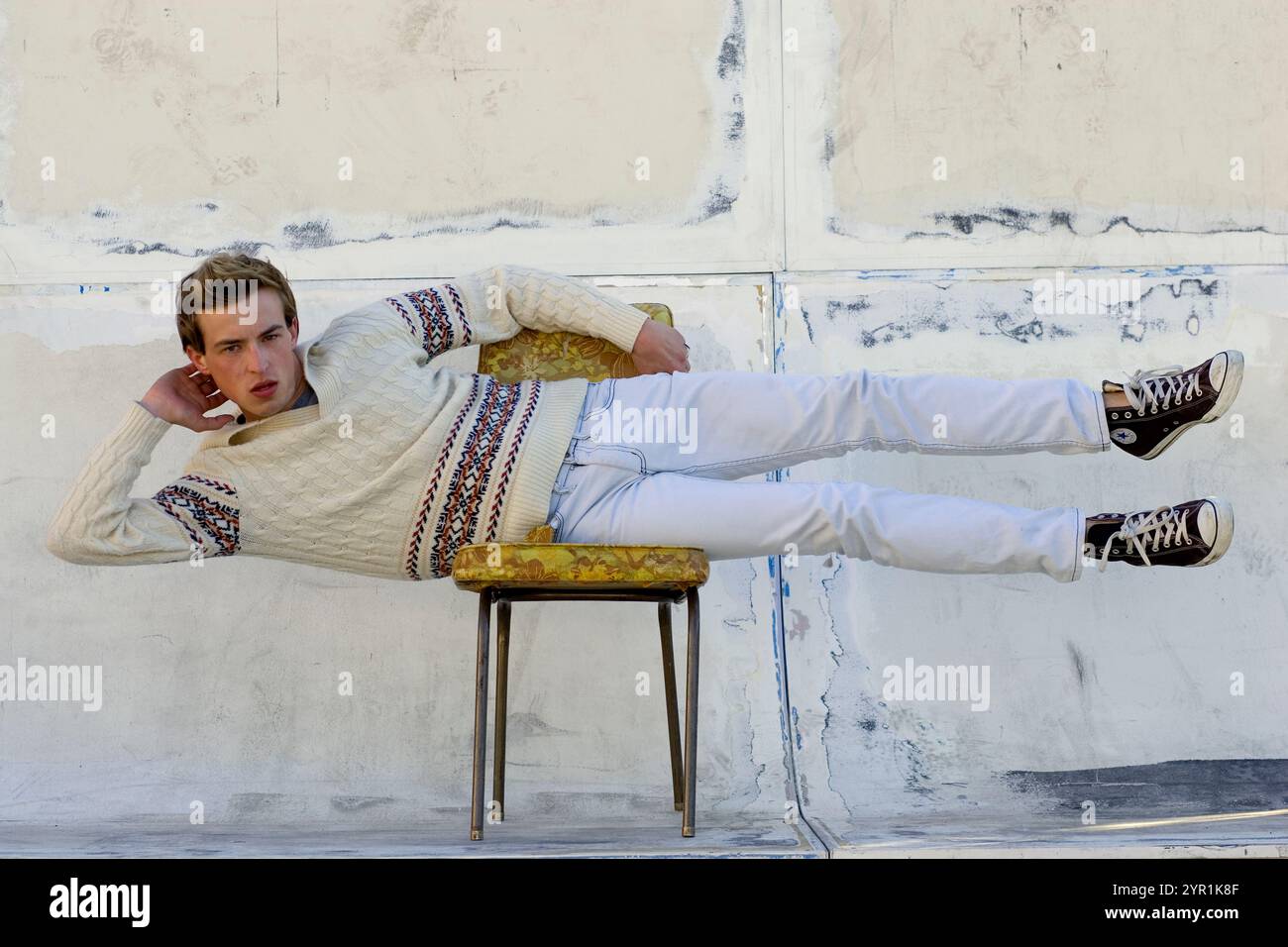 A male model lying horizontally across a chair during a photo shoot in ...