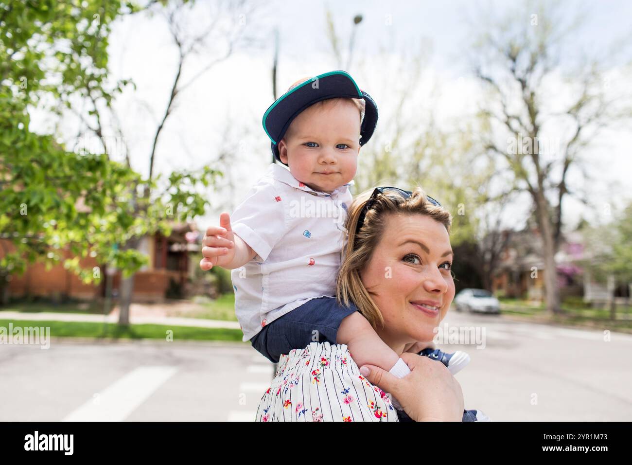 Happy mom smiles while giving toddler son in a hat a piggyback ride ...