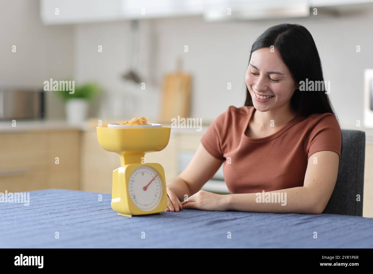 Happy asian woman weighing cereals using scale in the kitchen at home ...