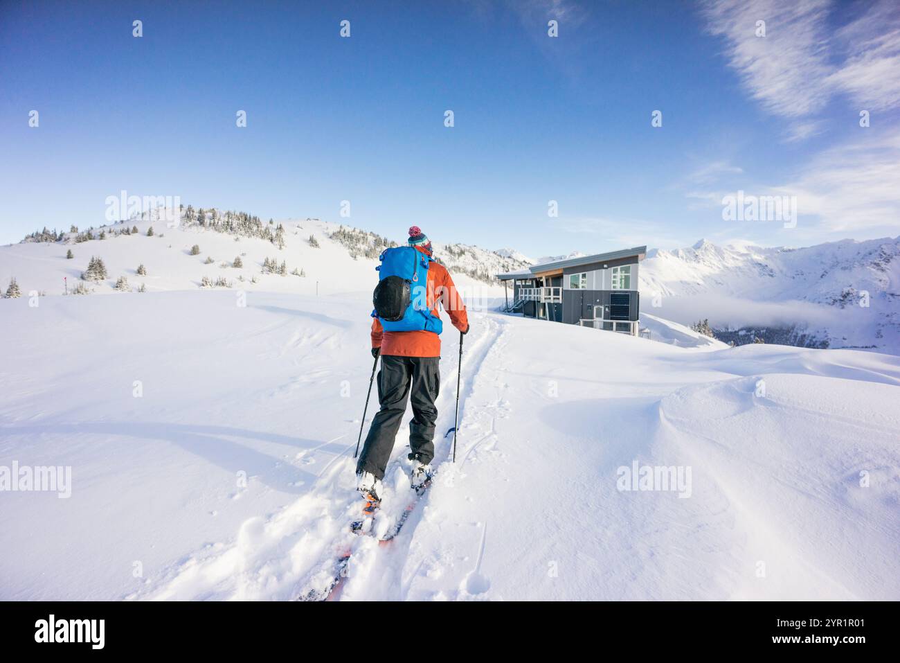 Rear view of skier touring towards remote mountain hut, Whistler B.C ...