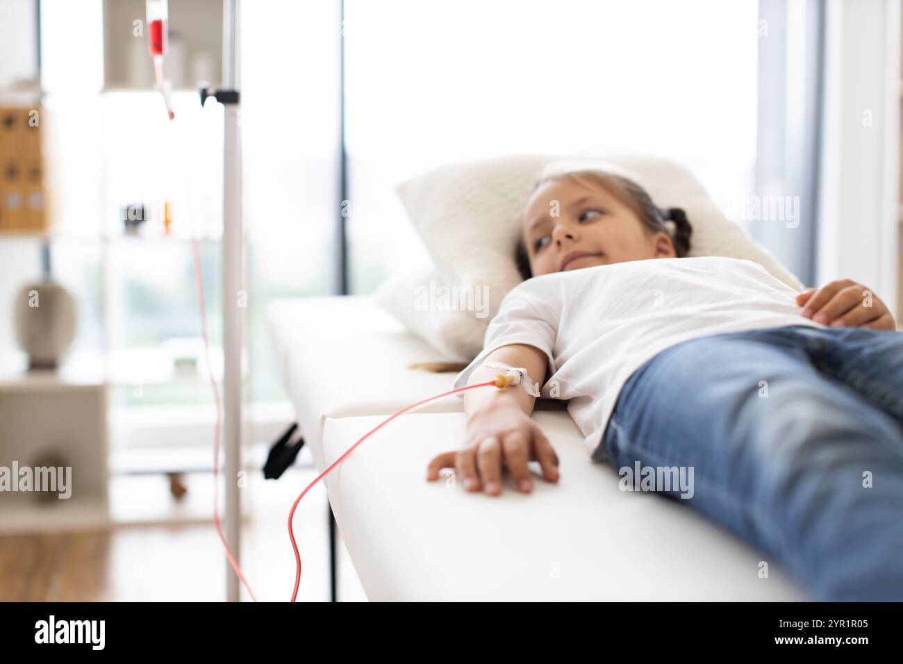 Young Caucasian girl lies on medical couch receiving blood transfusion ...