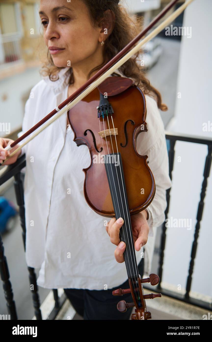 A woman is playing the violin on a balcony, focusing intently. Her ...