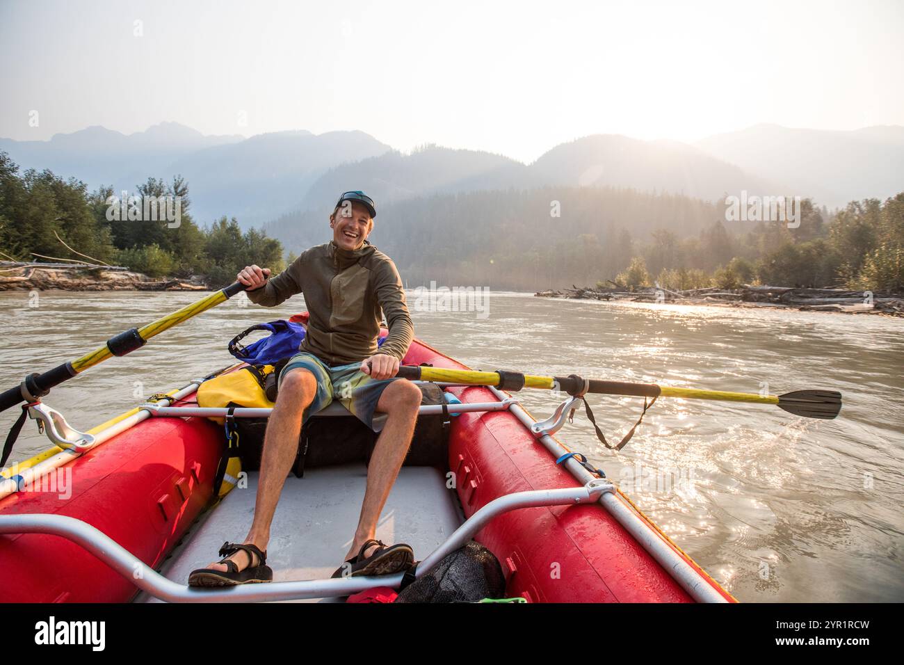 Guide smiles while rowing red inflatable raft on river at sunset Stock ...