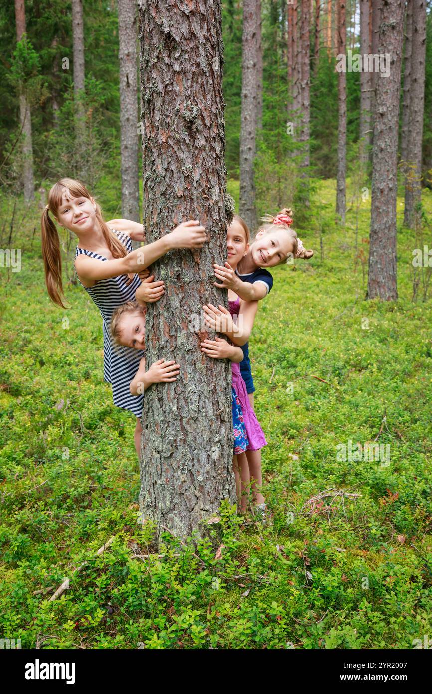 Four young girls hugging pine tree in the middle of a vibrant green ...