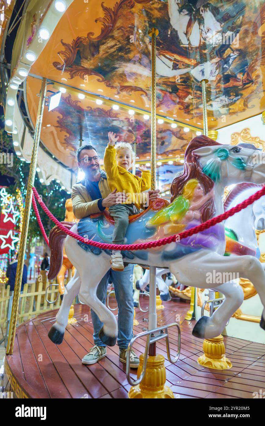 Father and son enjoying a carousel ride at a christmas market, waving ...