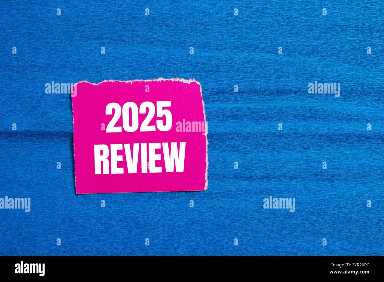 2025 review message written on ripped pink torn paper piece with blue background. Conceptual ...
