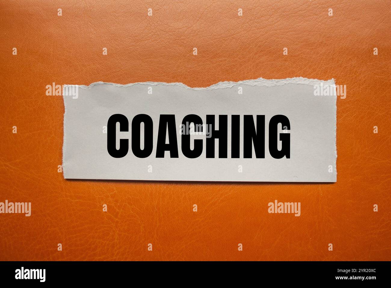 Coaching message written on ripped torn paper piece with brown background. Conceptual coaching ...