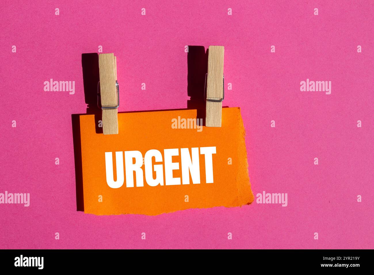 Urgent message written on ripped torn orange paper piece with pink ...