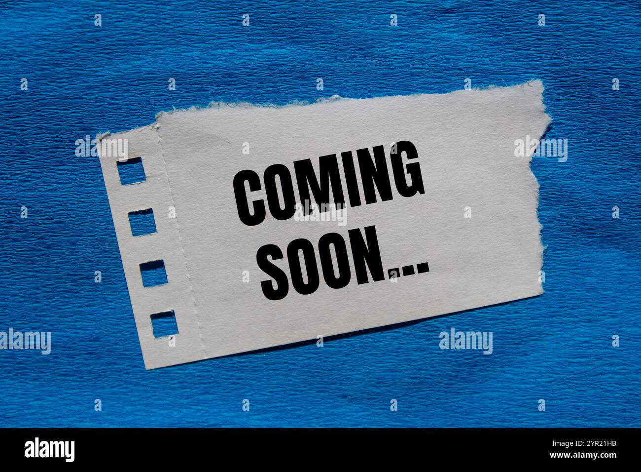 Coming soon message written on ripped torn paper piece with blue ...