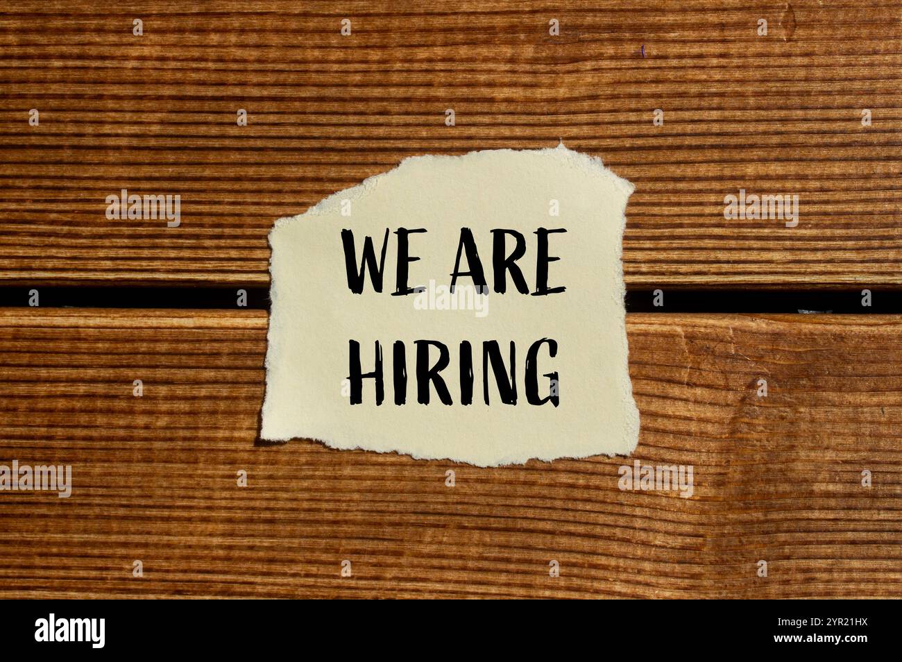 We are hiring message written on ripped torn paper with wooden background. Conceptual we are ...