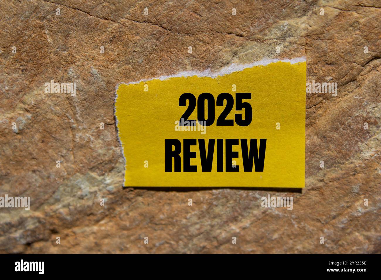 2025 review message written on ripped torn yellow paper piece with stone background. Conceptual ...