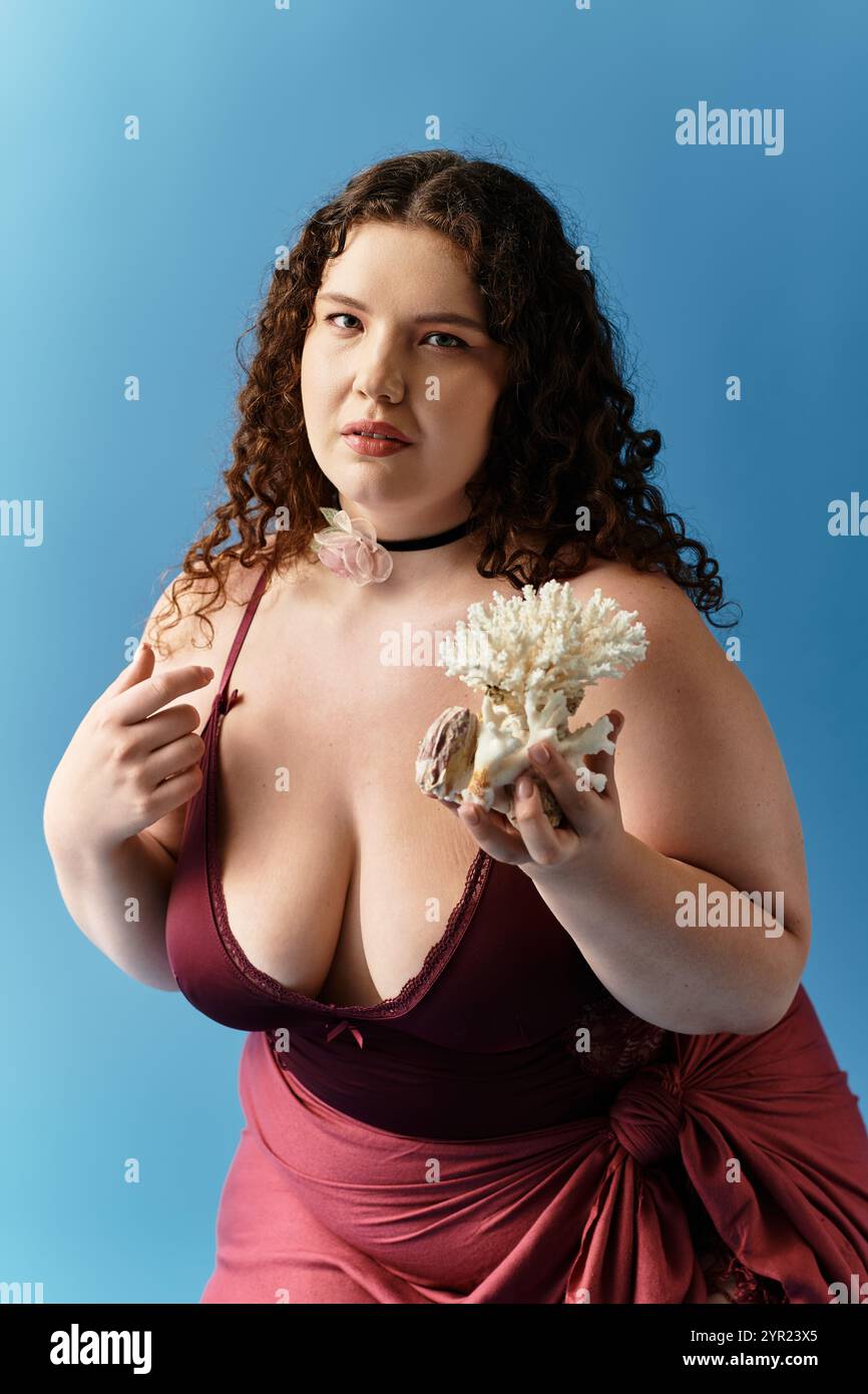 Charming young woman in trendy attire poses elegantly while holding a stunning shell Stock Photo ...