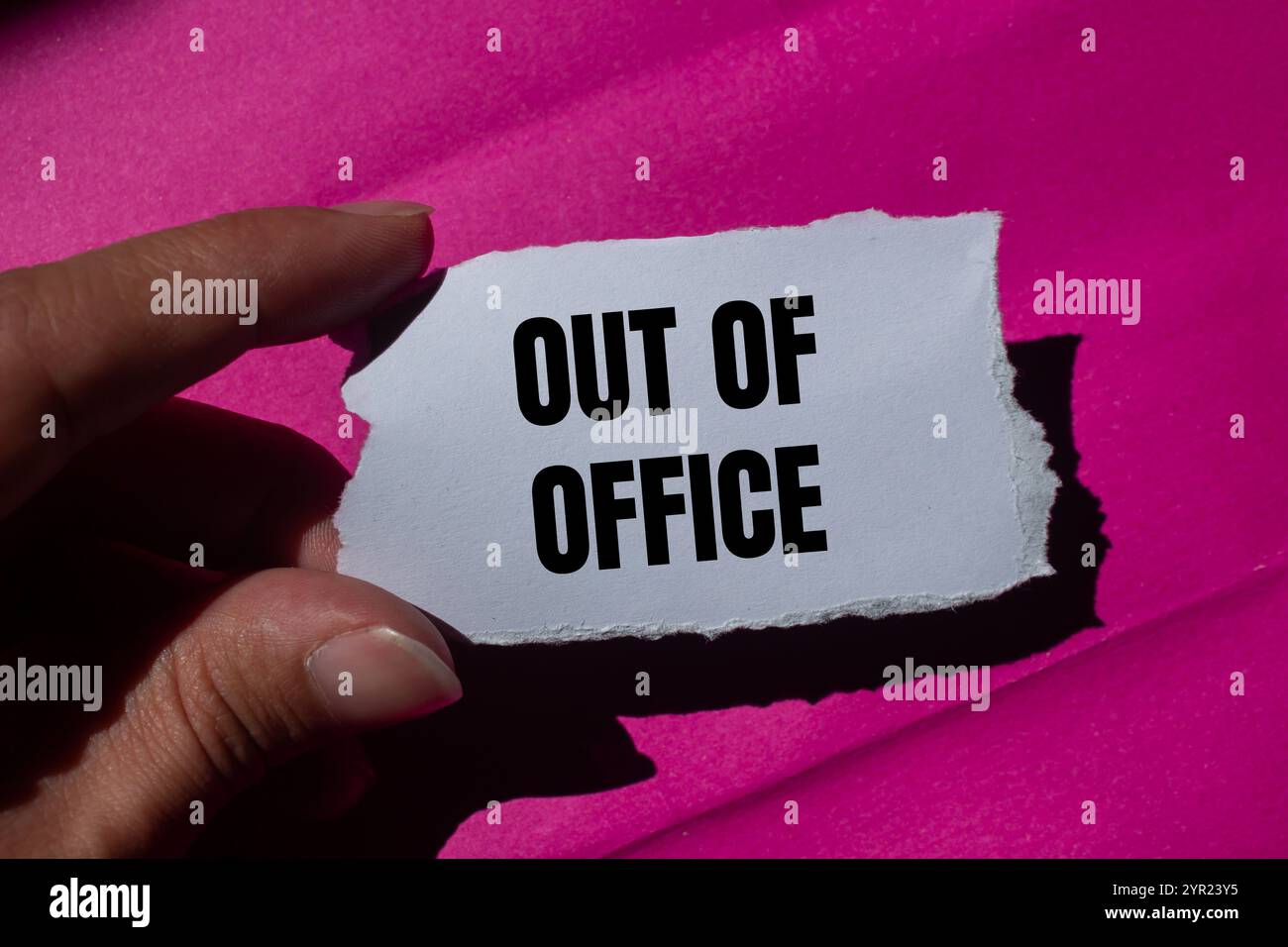 Out of office message written on ripped torn paper piece with a pink ...