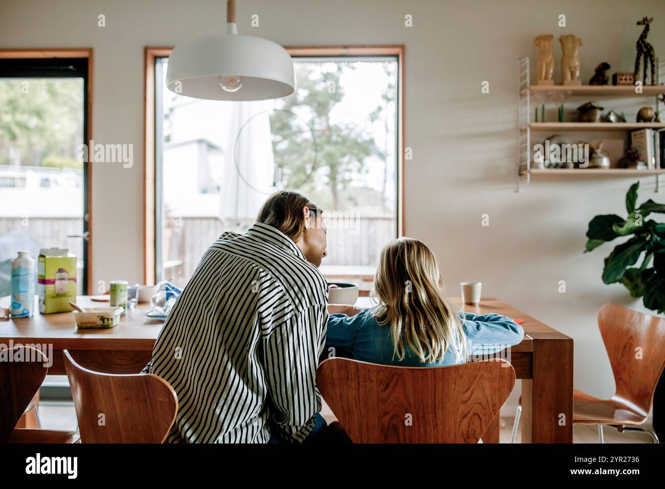 Rear view mother guiding son doing homework while sitting on chair near ...