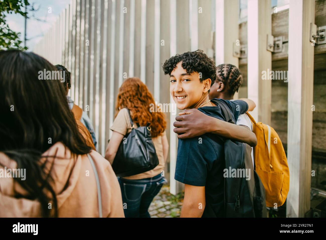 Portrait of smiling teenage boy walking with arm around friend near ...