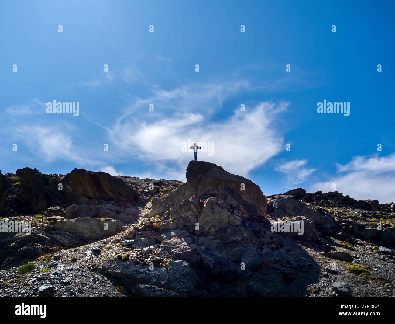 Black cross standing on top of cliff rock formation on blue sky ...