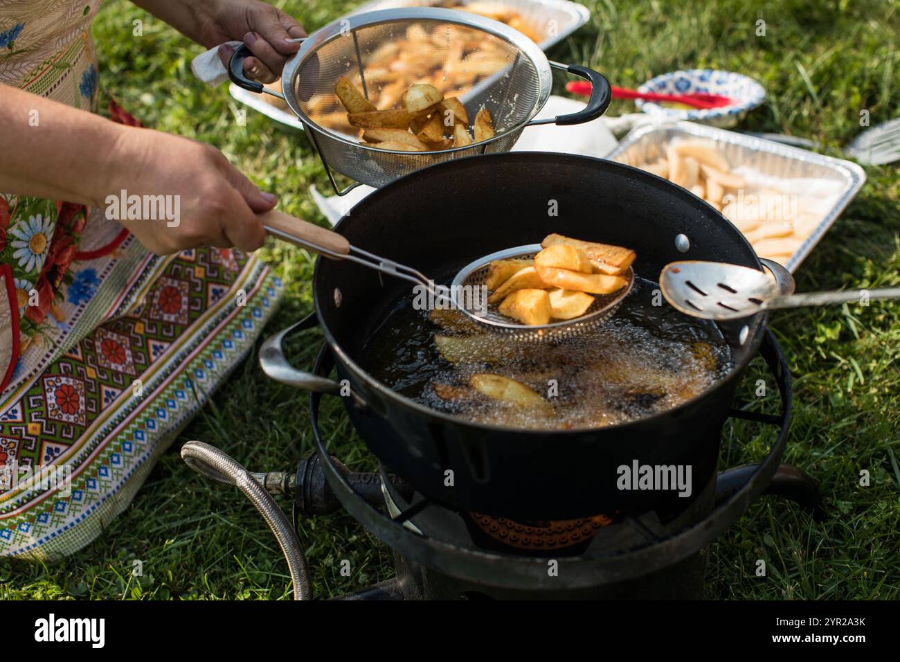 A woman frying potatoes in a cauldron outdoors Stock Photo - Alamy