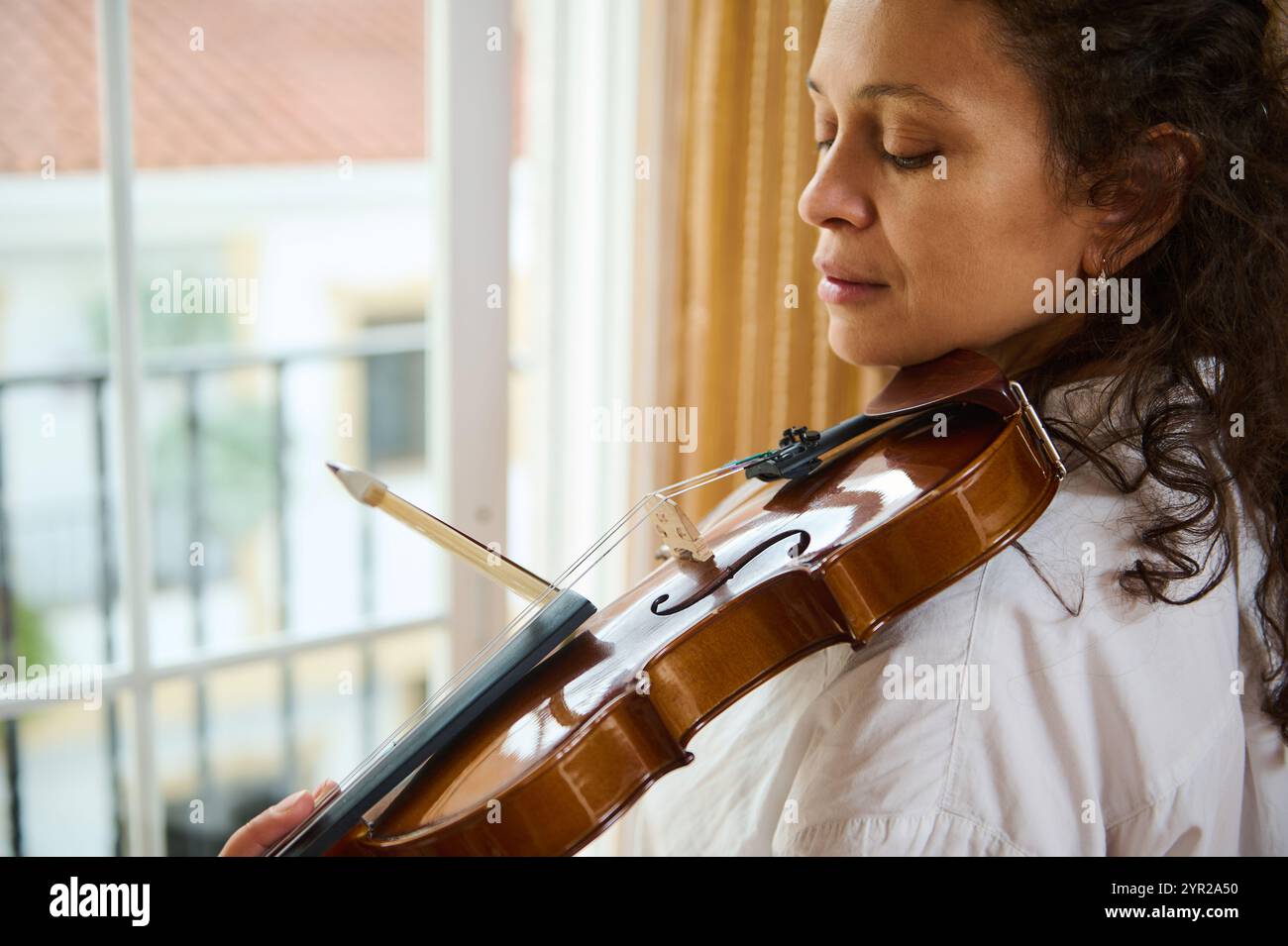 A woman plays the violin near a bright window, embracing a moment of ...
