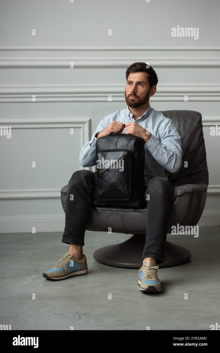 A man is comfortably sitting in a chair, resting with a leather ...