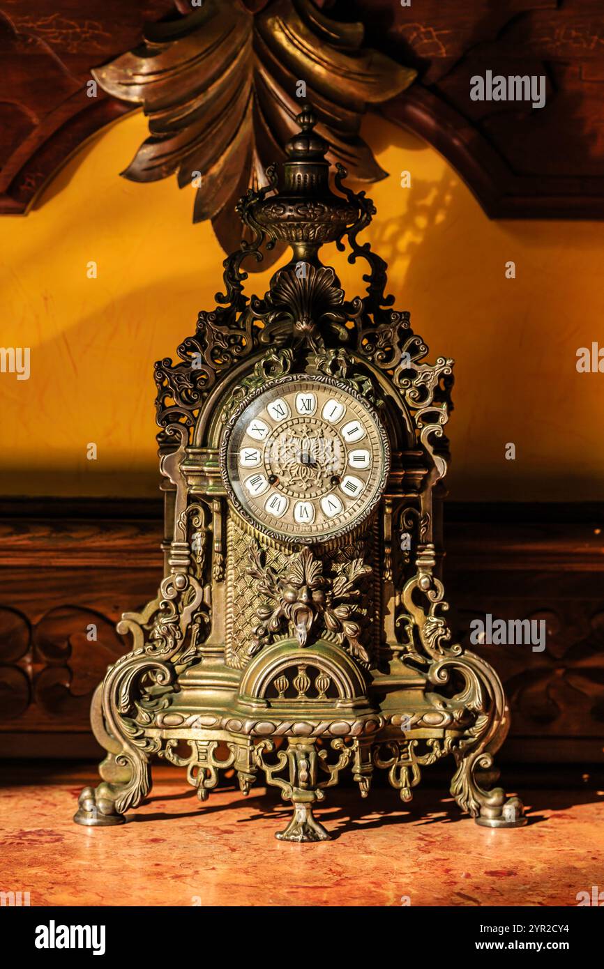 A large, ornate clock with a gold frame sits on a table. The clock has ...