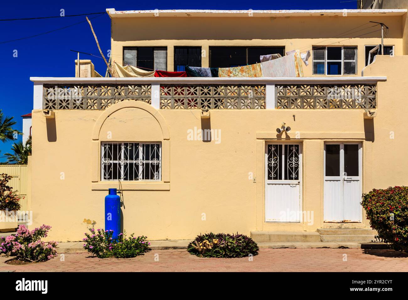 A yellow house with a blue water tank on the side. The house has a ...