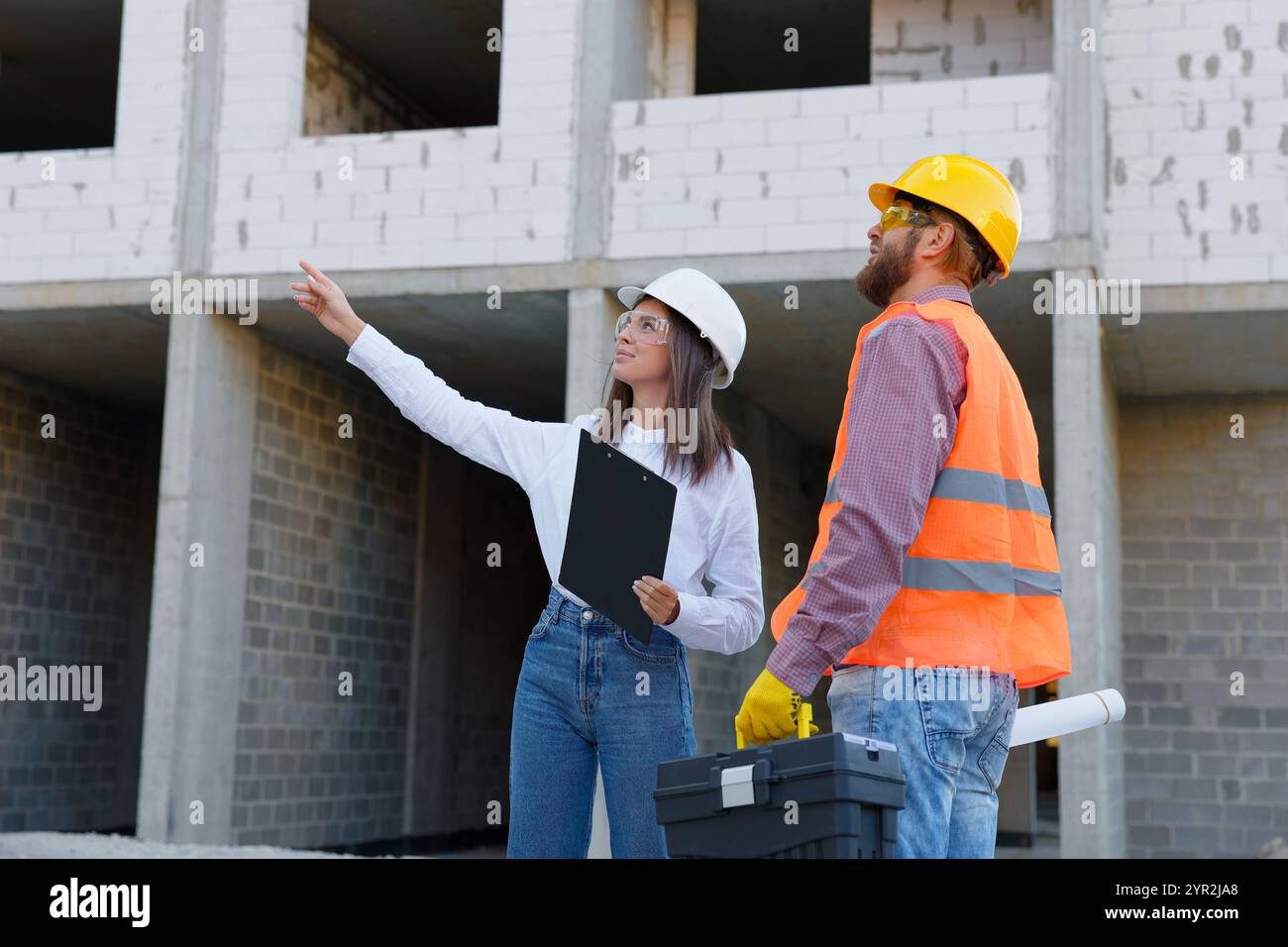 Architect and construction worker wearing safety helmets and discussing building project details ...