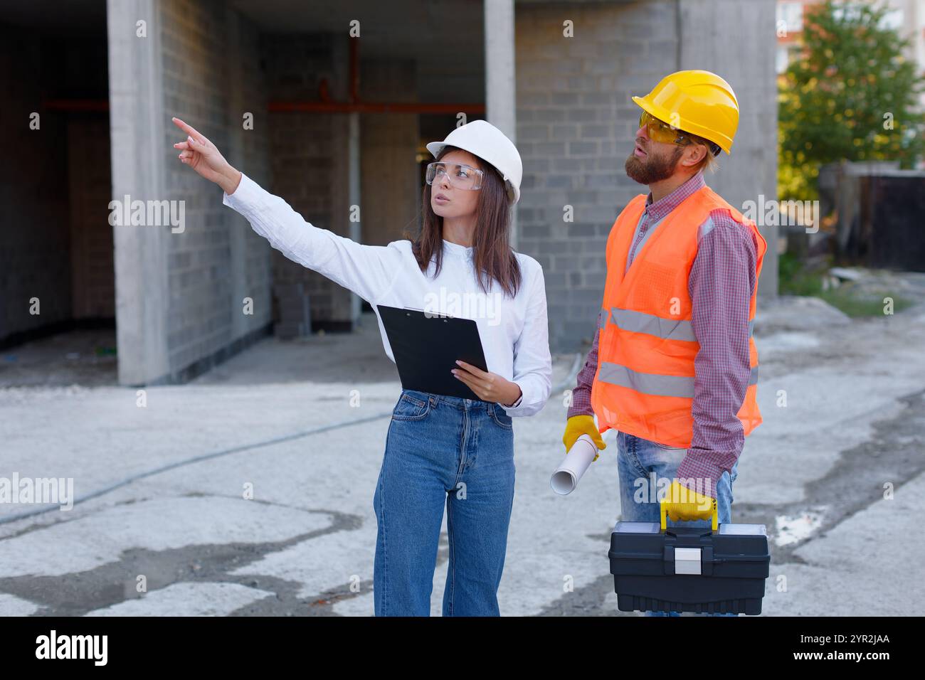 Architect and construction worker wearing safety helmets and discussing building project details ...