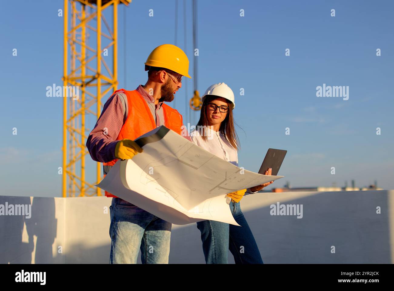 Construction workers reviewing blueprints on a building site with crane ...
