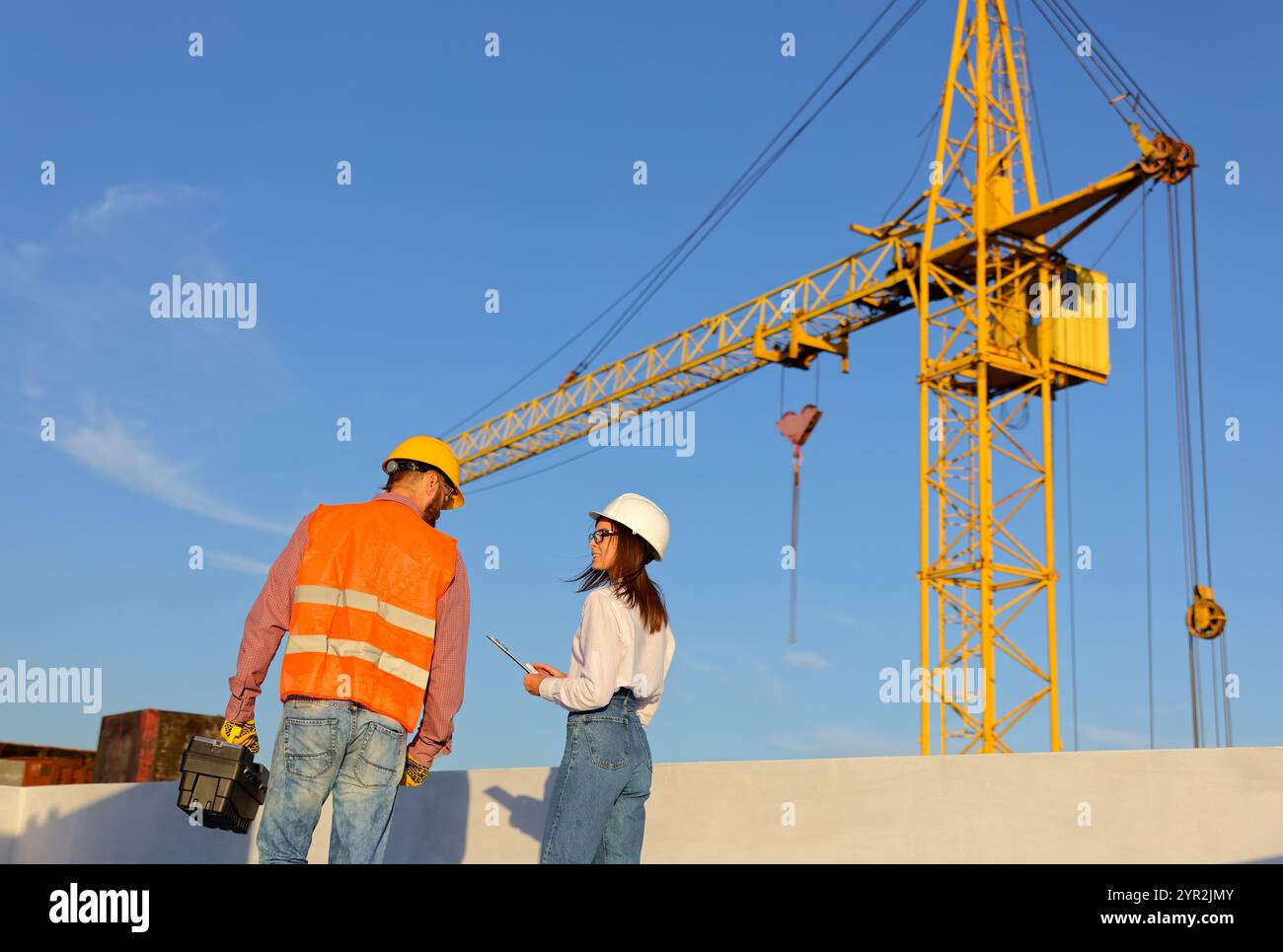Construction workers reviewing blueprints on a building site, discussing progress with crane in ...