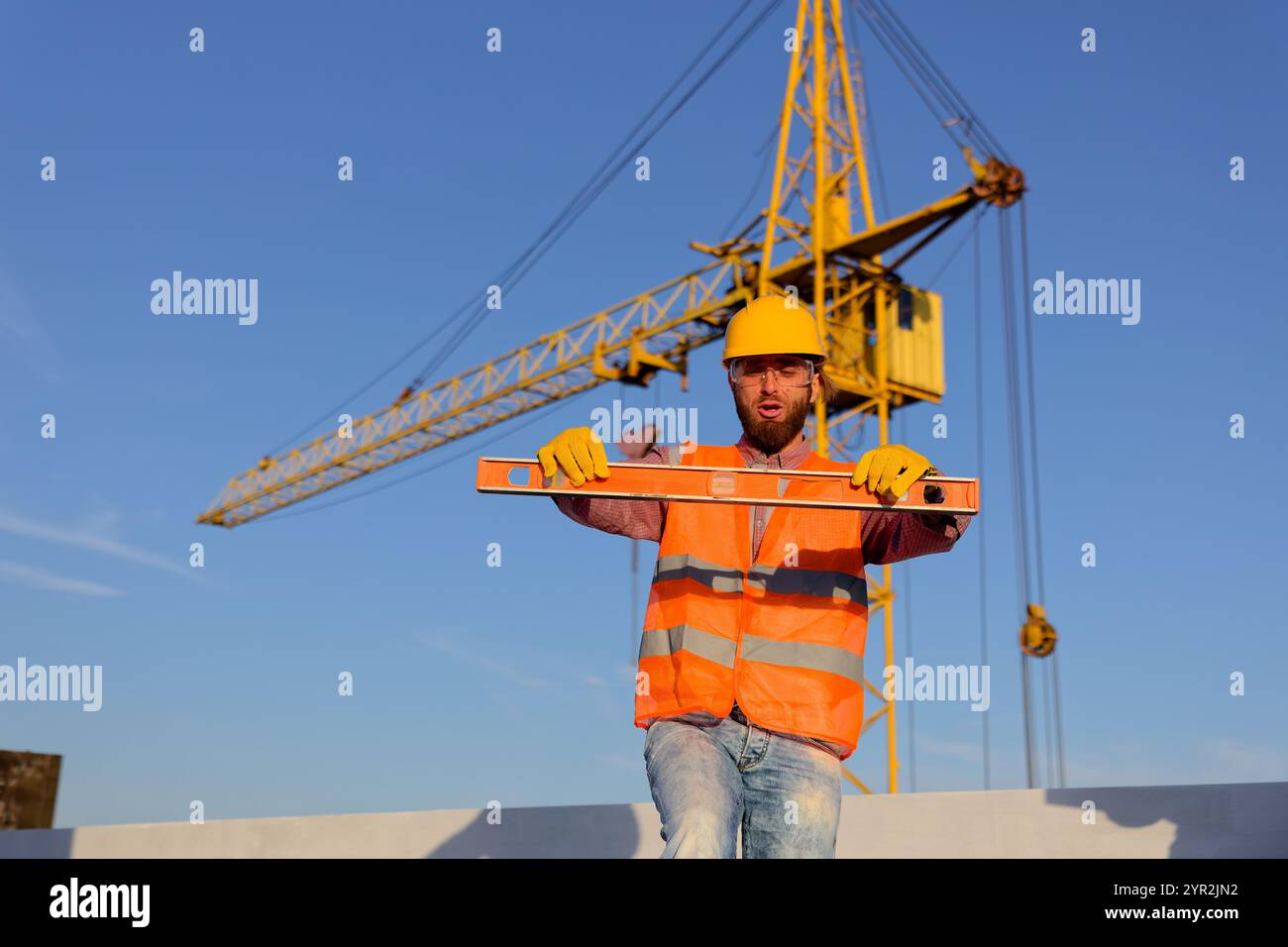 Builder using spirit level at construction site with crane in ...