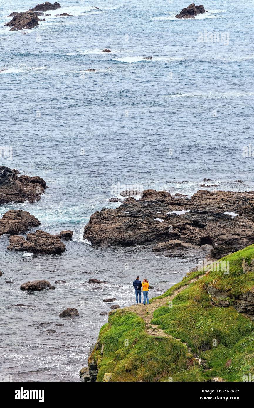 The treacherous rocky coastline at Lizard Point with a young couple ...
