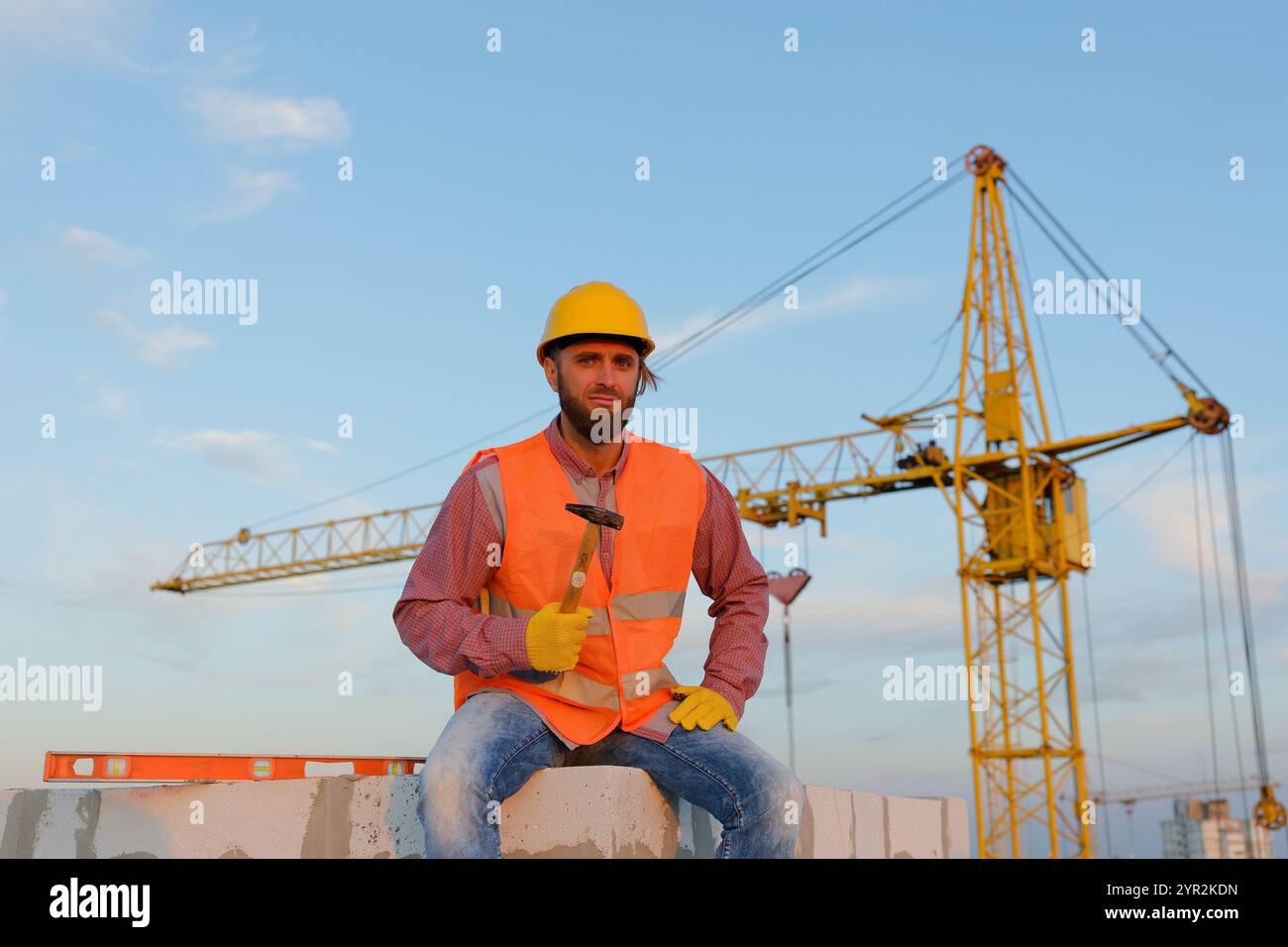 Construction worker holding a hammer, sitting on a concrete block at a ...