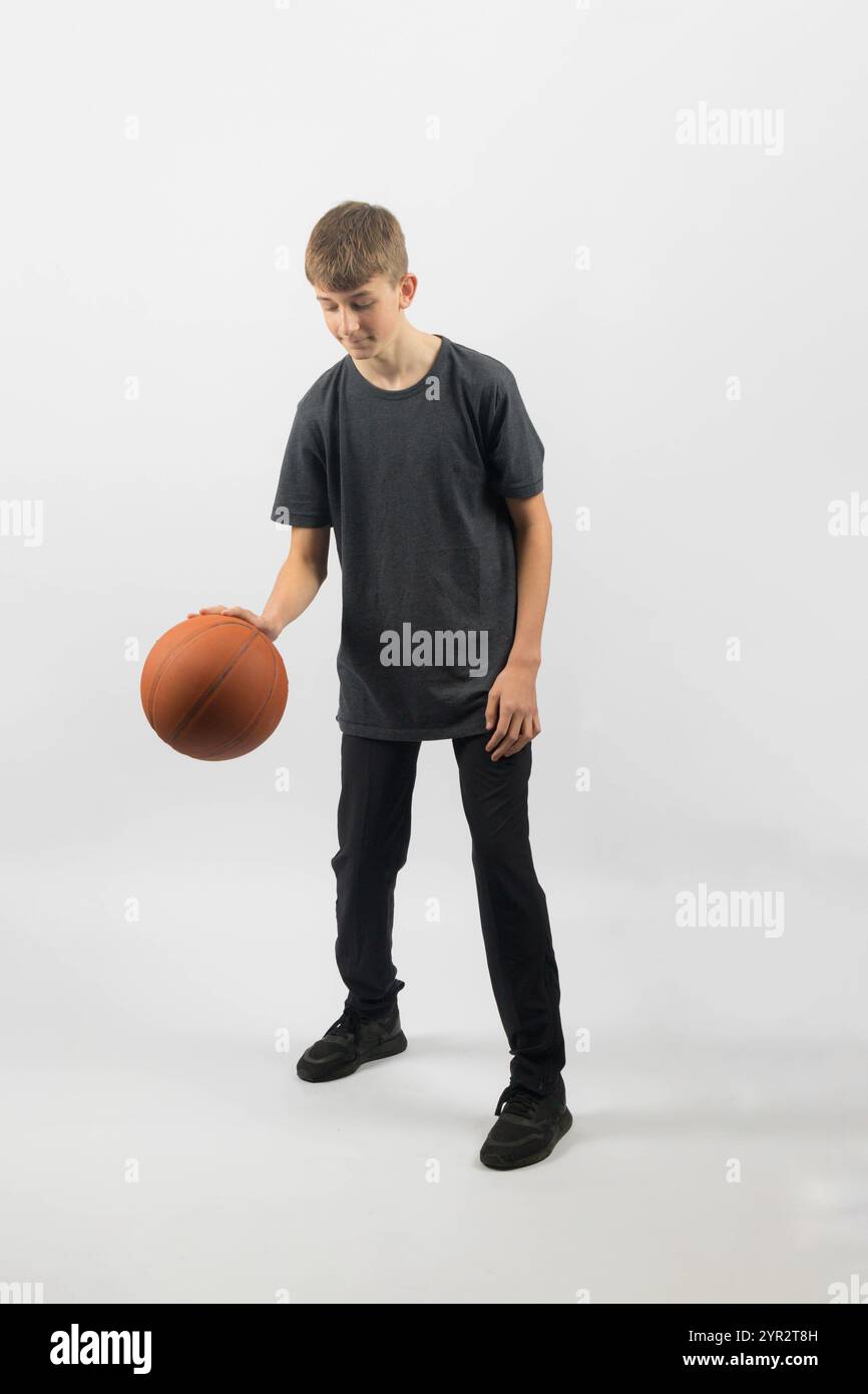 Fifteen year old teenage boy bouncing a basketball, studio shot against ...