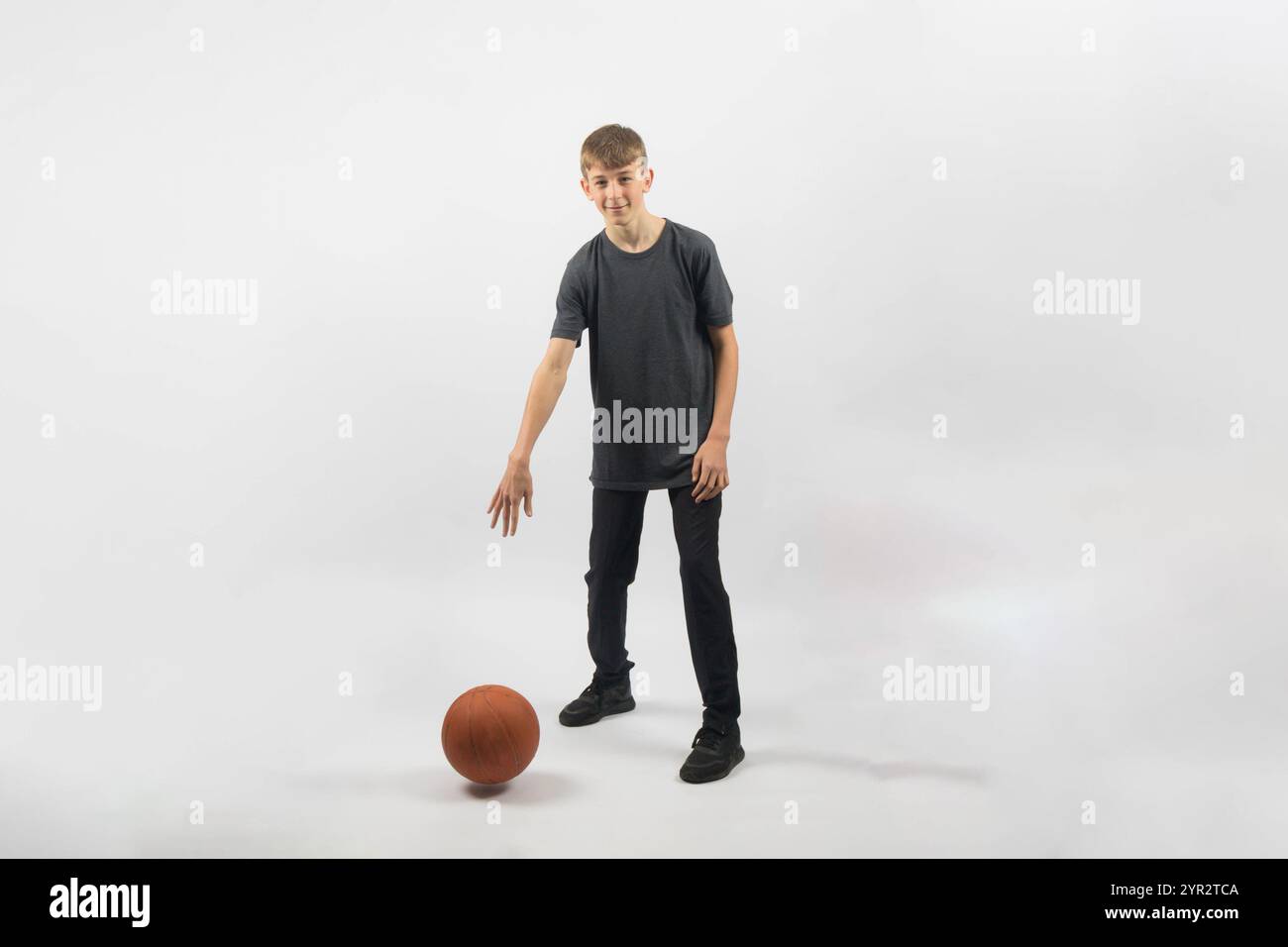 Fifteen year old teenage boy bouncing a basketball, studio shot against ...