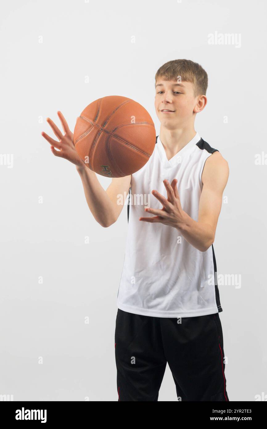 Fifteen year old teenage boy catching a basketball, studio shot against ...
