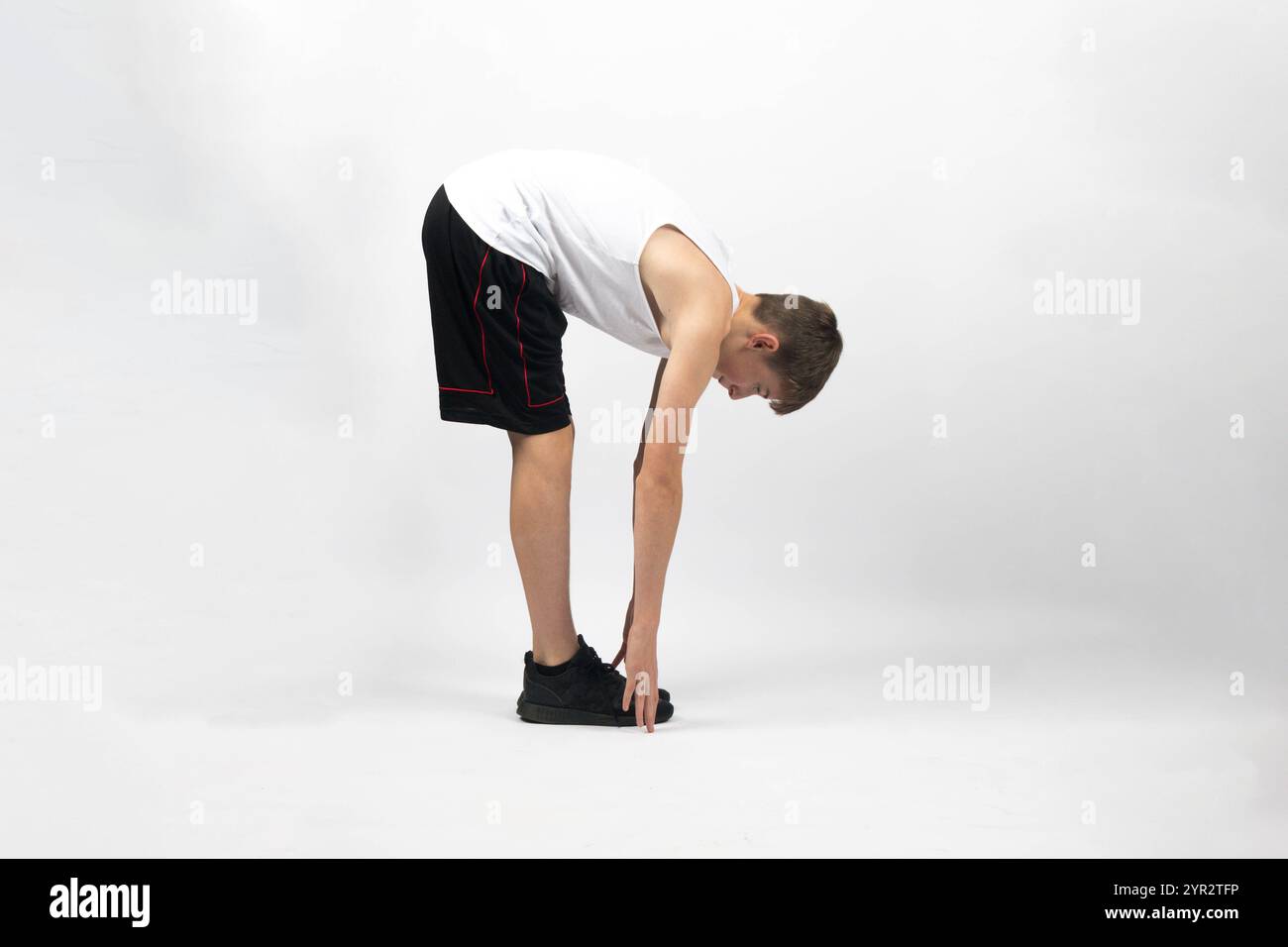 Fifteen year old teenage boy touching his toes, studio shot against a ...