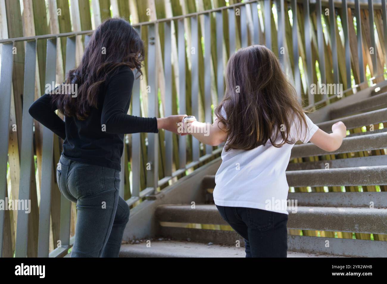 Two sisters holding hands climb up the steps in a summer park. Concept ...