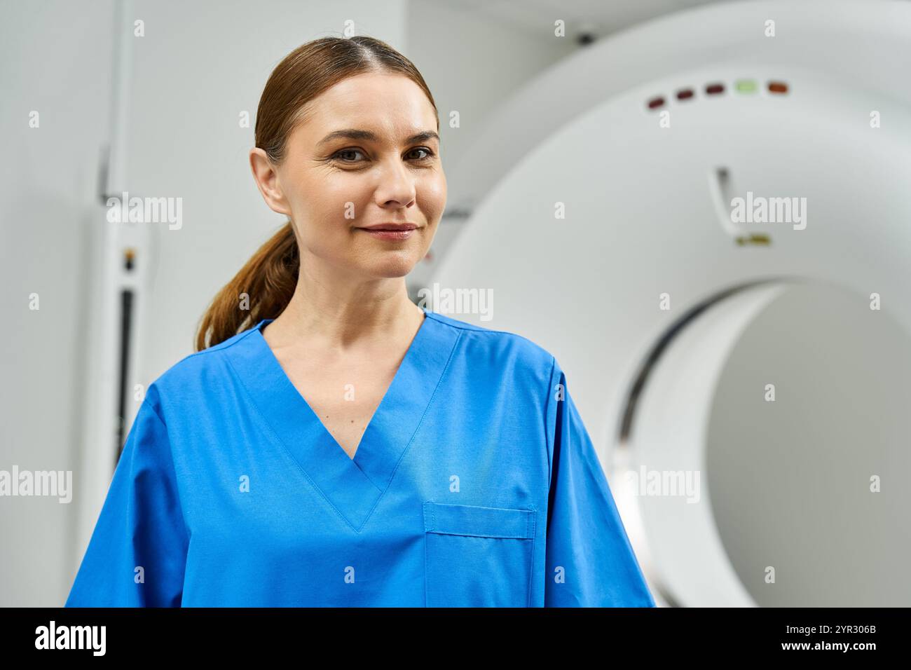 Female doctor in blue scrubs stands ready next to an MRI machine in a ...