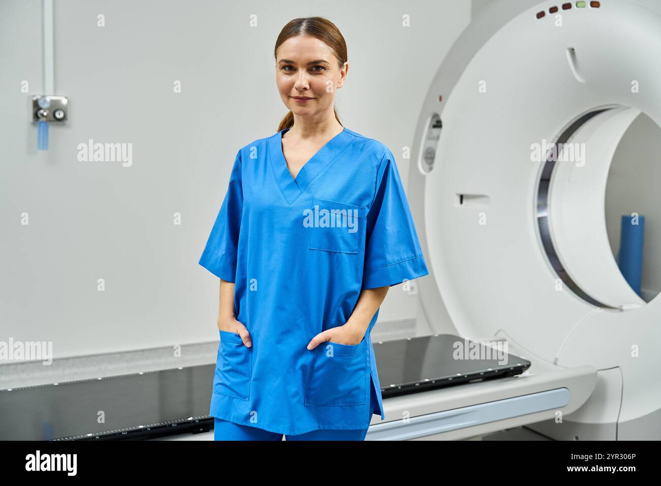 Confident female doctor in blue scrubs stands by an MRI machine, ready ...