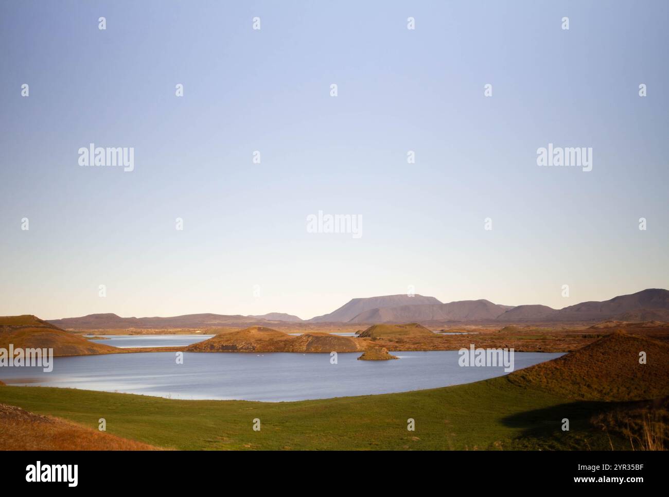 A calm lake nestled in the middle of a vast, open field, surrounded by ...